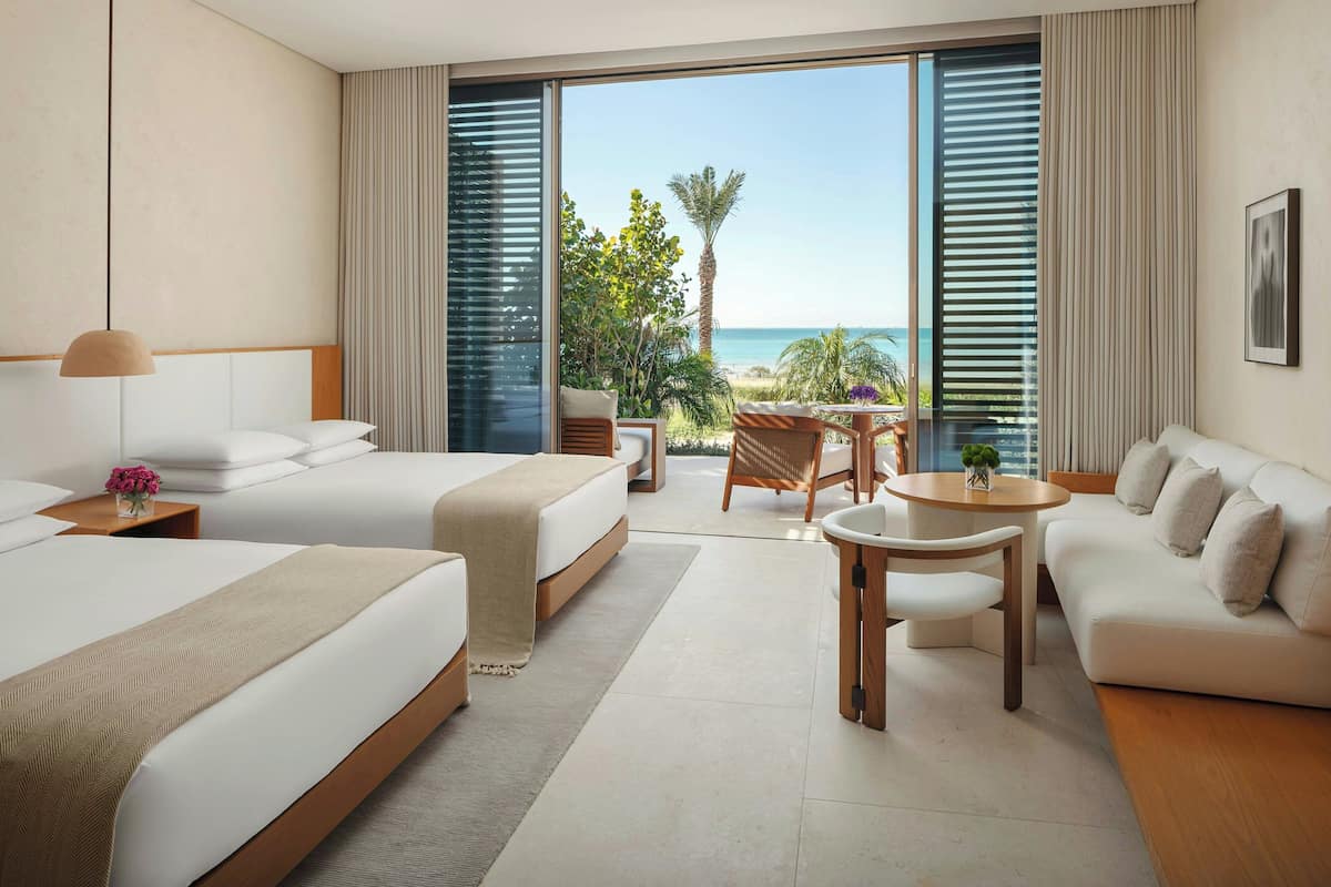 Quarto de hotel com duas camas, um sofá, uma mesa de jantar e vista para a praia.