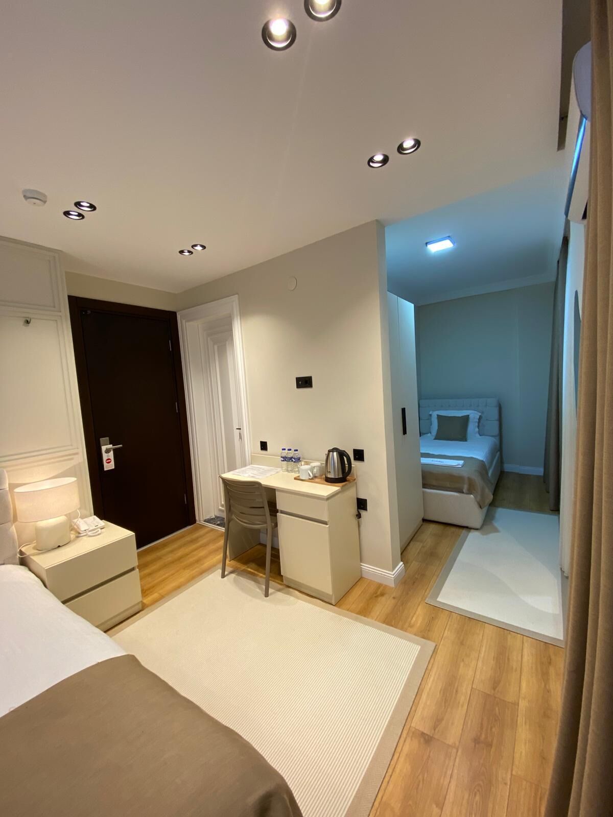 Quarto de hotel com cama, escrivaninha, cadeira, mesa de cabeceira e uma pequena área de cozinha.