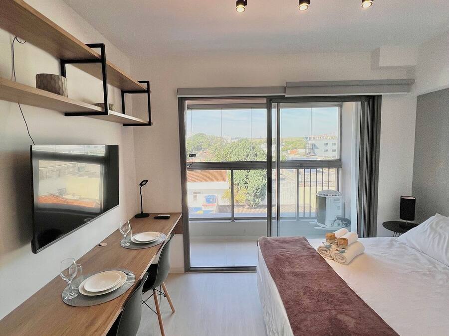 Quarto de hotel moderno com cama, escrivaninha com televisão, área de refeições e varanda com vista.
