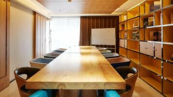 Uma sala de conferências com uma mesa comprida, cadeiras, um quadro branco e uma estante de livros.