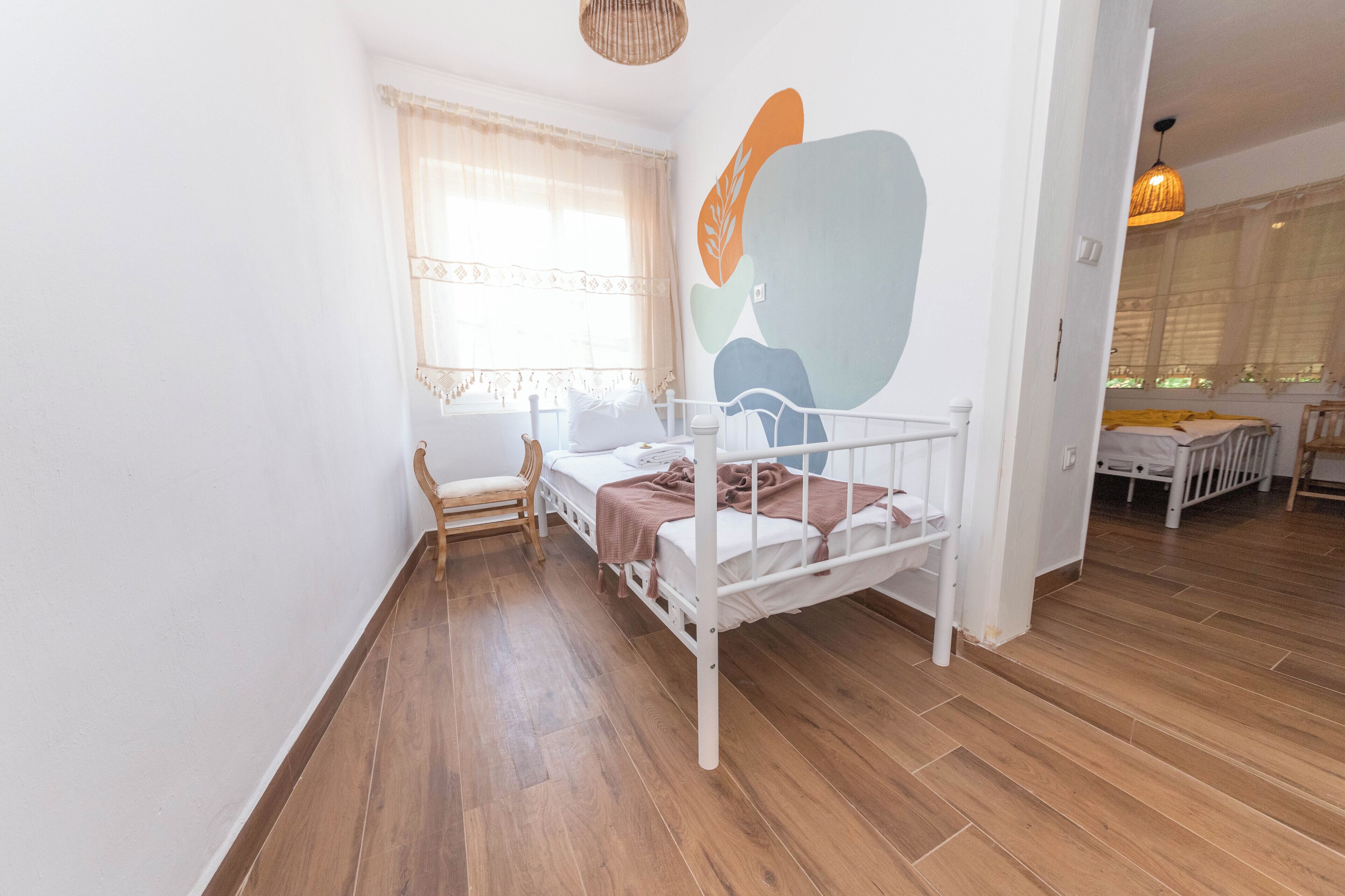 Quarto de criança com beliche, piso de madeira, janela com cortinas e um mural na parede.