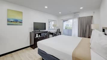Quarto de hotel com uma cama, uma escrivaninha com computador, televisão e um quadro na parede.