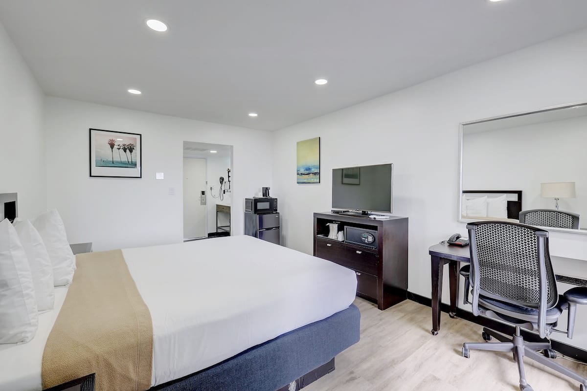 Quarto de hotel com cama, escrivaninha com cadeira, televisão, micro-ondas e frigorífico.