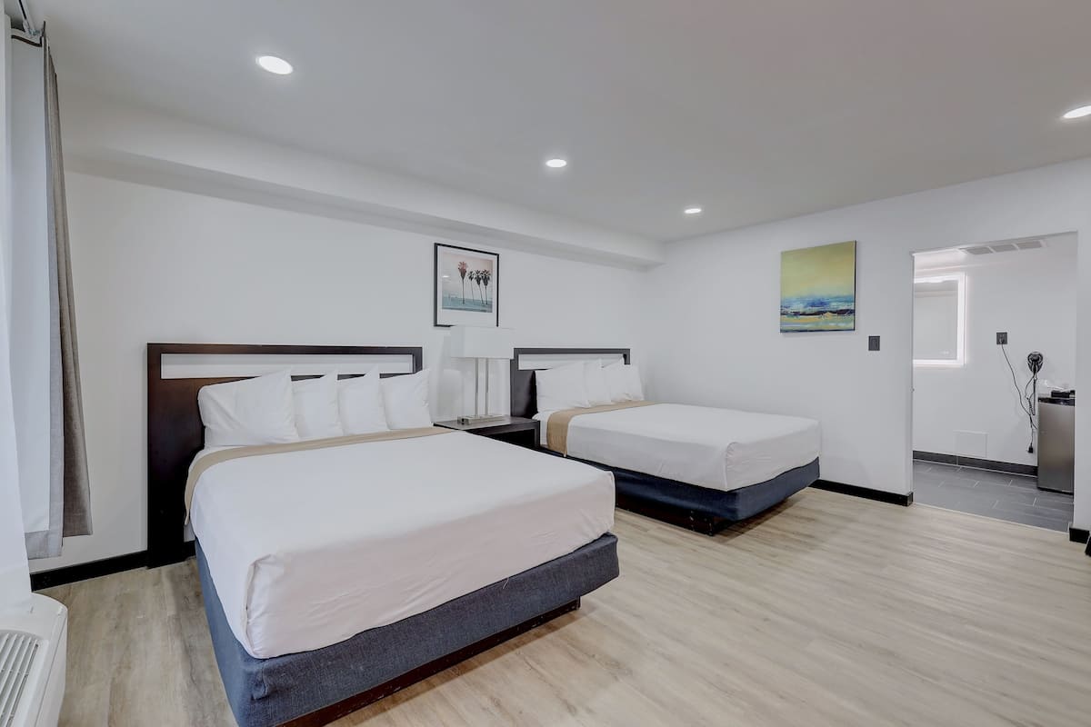 Quarto de hotel com duas camas de solteiro, uma janela grande e um banheiro visível ao fundo.