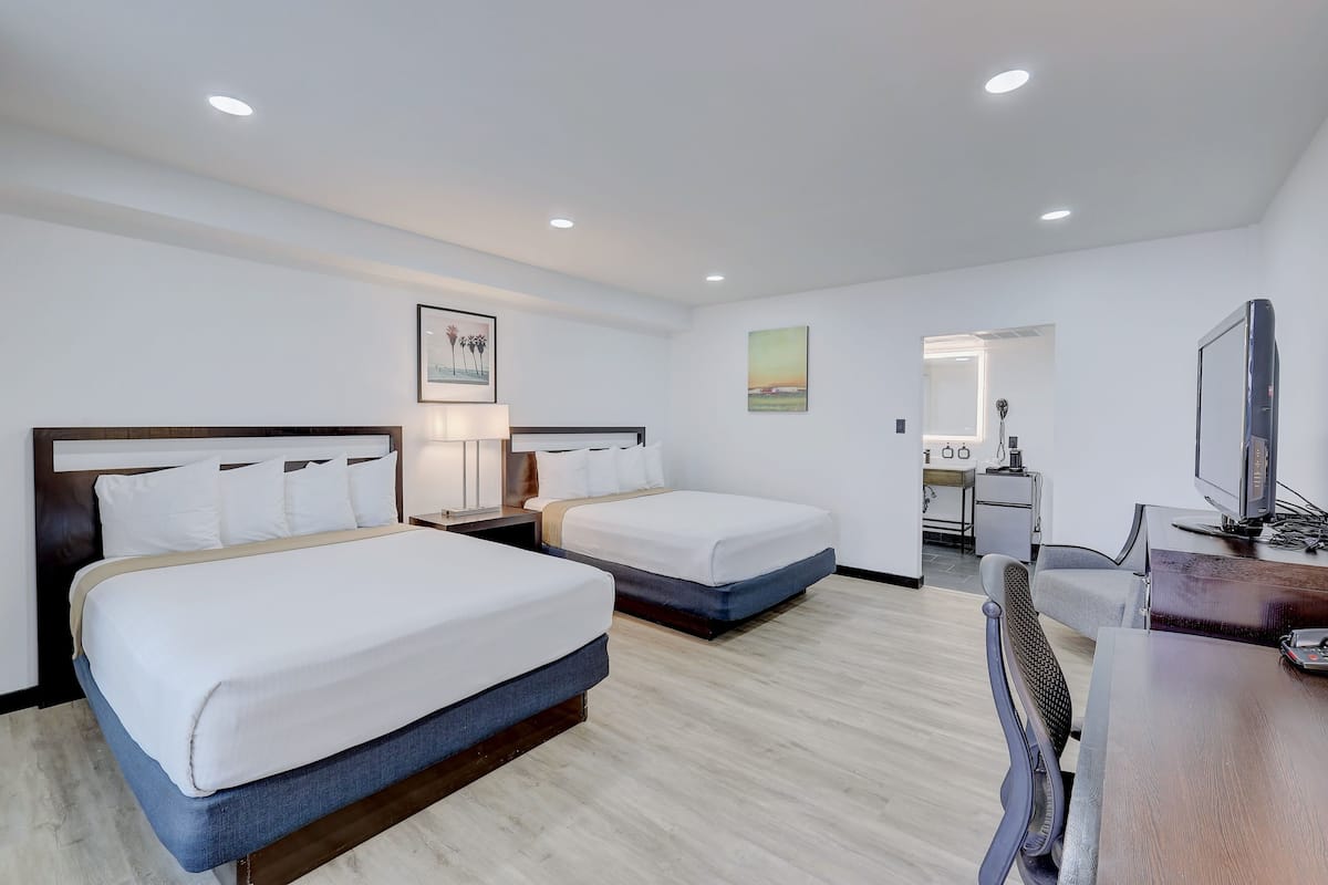 Quarto de hotel com duas camas, uma escrivaninha, uma cadeira e uma televisão.