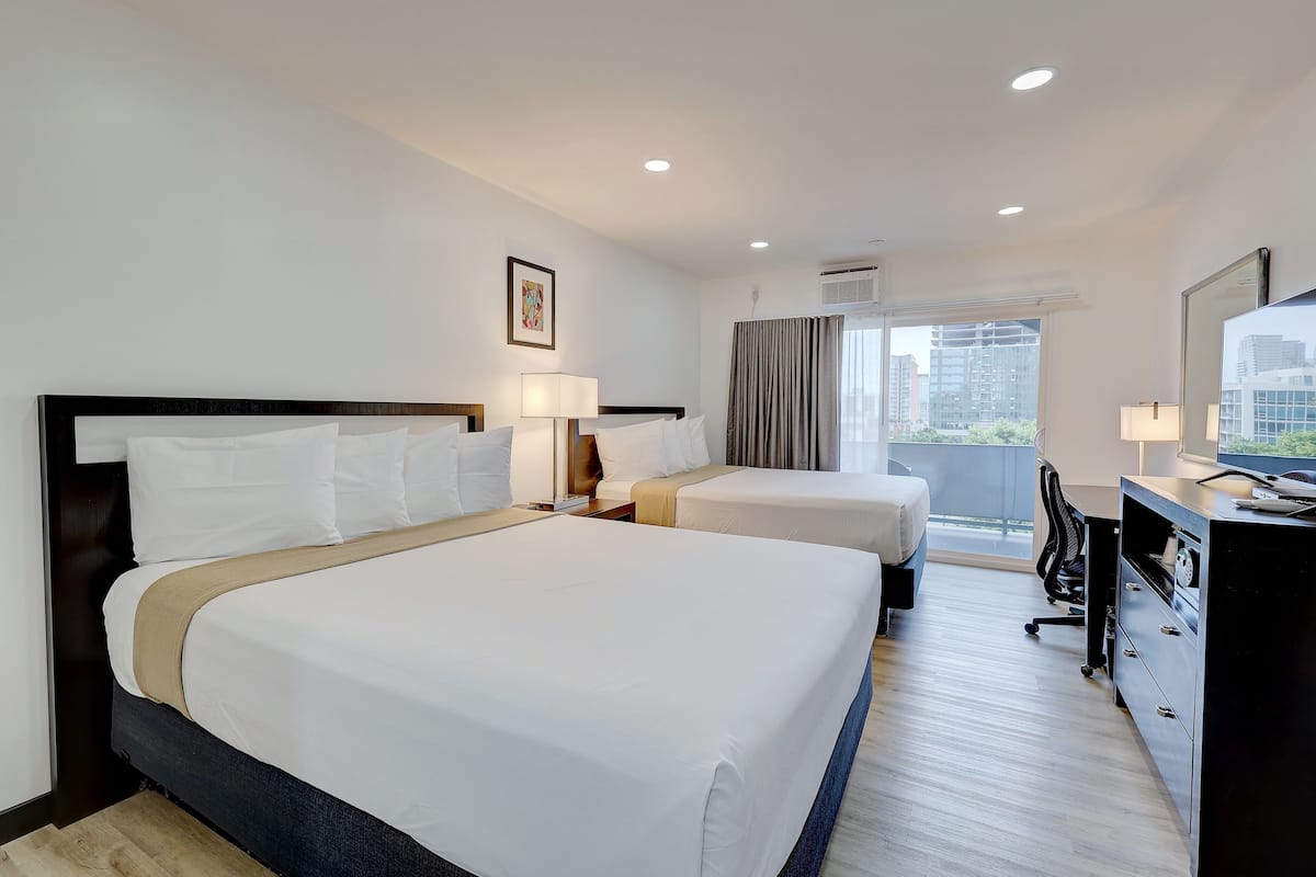 Quarto de hotel com duas camas, uma mesa, uma cadeira e uma janela grande com vista para a cidade.