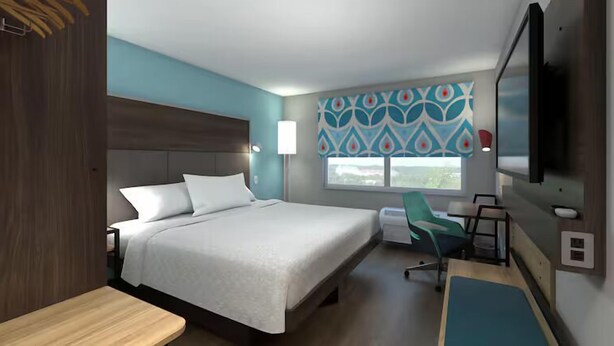 Quarto de hotel com cama, escrivaninha, cadeira, televisão e janela com vista.