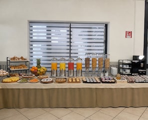 Buffet com diversos alimentos, dispensadores de suco e uma máquina de café.