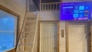 Interior em madeira com escada, uma TV exibindo a interface Roku TV e uma porta.