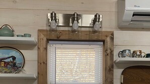 Uma cozinha com pia de aço inoxidável, uma janela com persianas e uma cafeteira no balcão.