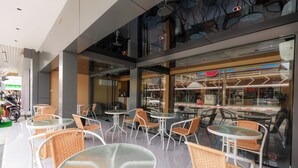 Um café moderno e acolhedor, com mesas redondas e cadeiras de vime, fachada em vidro e vista para a rua.