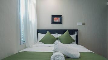Cama bem arrumada com roupa de cama e almofadas verdes, toalha branca enrolada na cama e um quadro na parede.