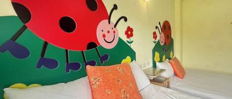 Quarto de hotel com cama, almofadas, mesa de cabeceira e um ornamento de parede com um joaninha.