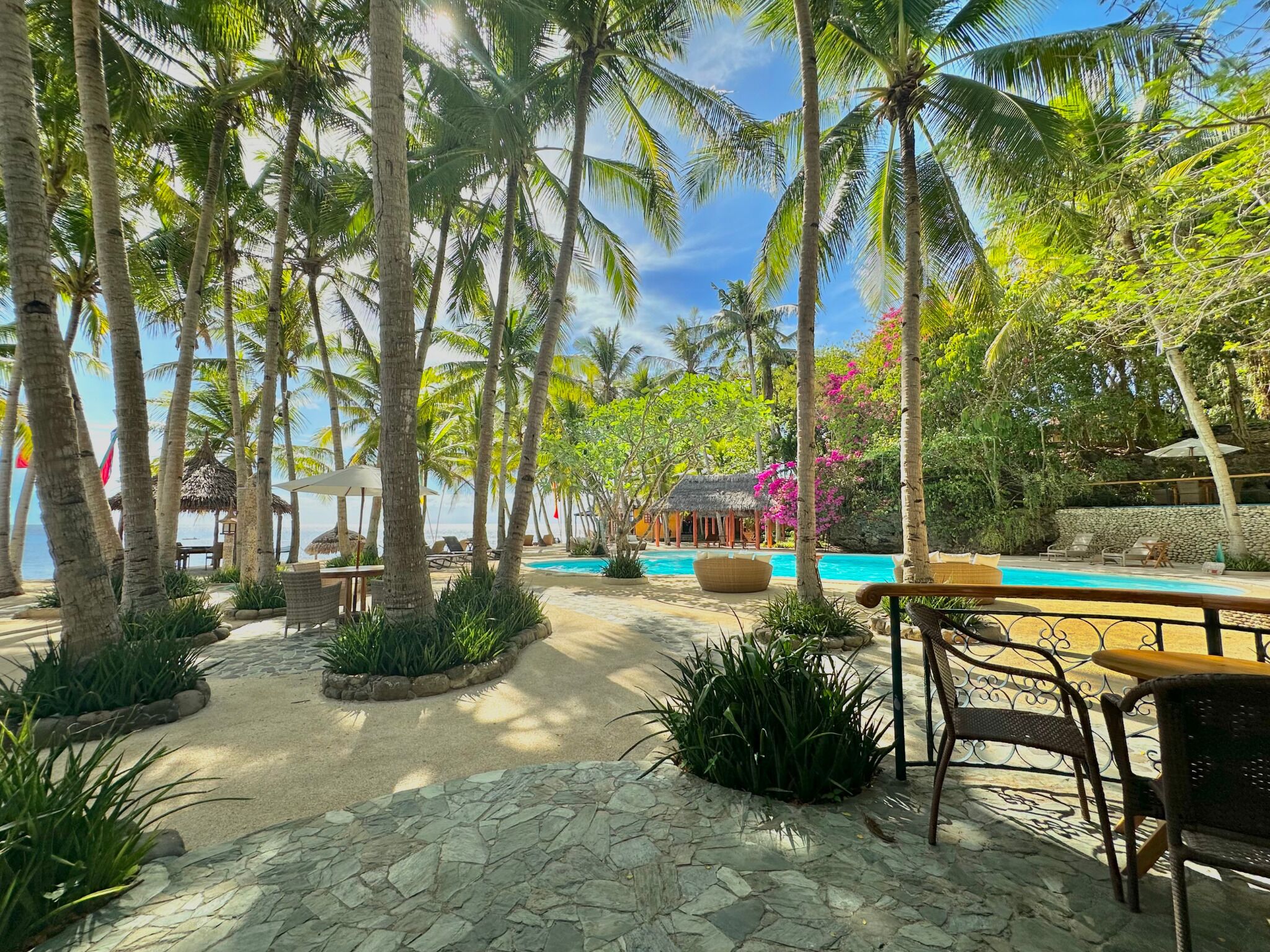 Um resort tropical com piscina, palmeiras e áreas de estar ao ar livre.