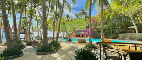 Um resort tropical com piscina, palmeiras e áreas de estar ao ar livre.