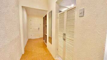 Um corredor com piso coberto por carpete, uma porta branca e um armário com portas venezianas.