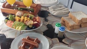Uma mesa de jantar com vários pratos, incluindo salsichas, batatas fritas e uma travessa de frutas.