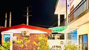 Um edifício de dois andares com fachada de tijolos vermelhos, varanda no andar superior e um pátio com plantas em vasos.