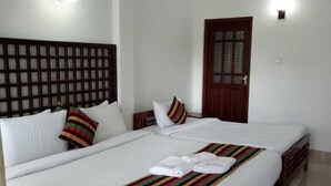 Quarto de hotel com cama grande, cabeceira de madeira, ventilador de teto e porta com painel de vidro.