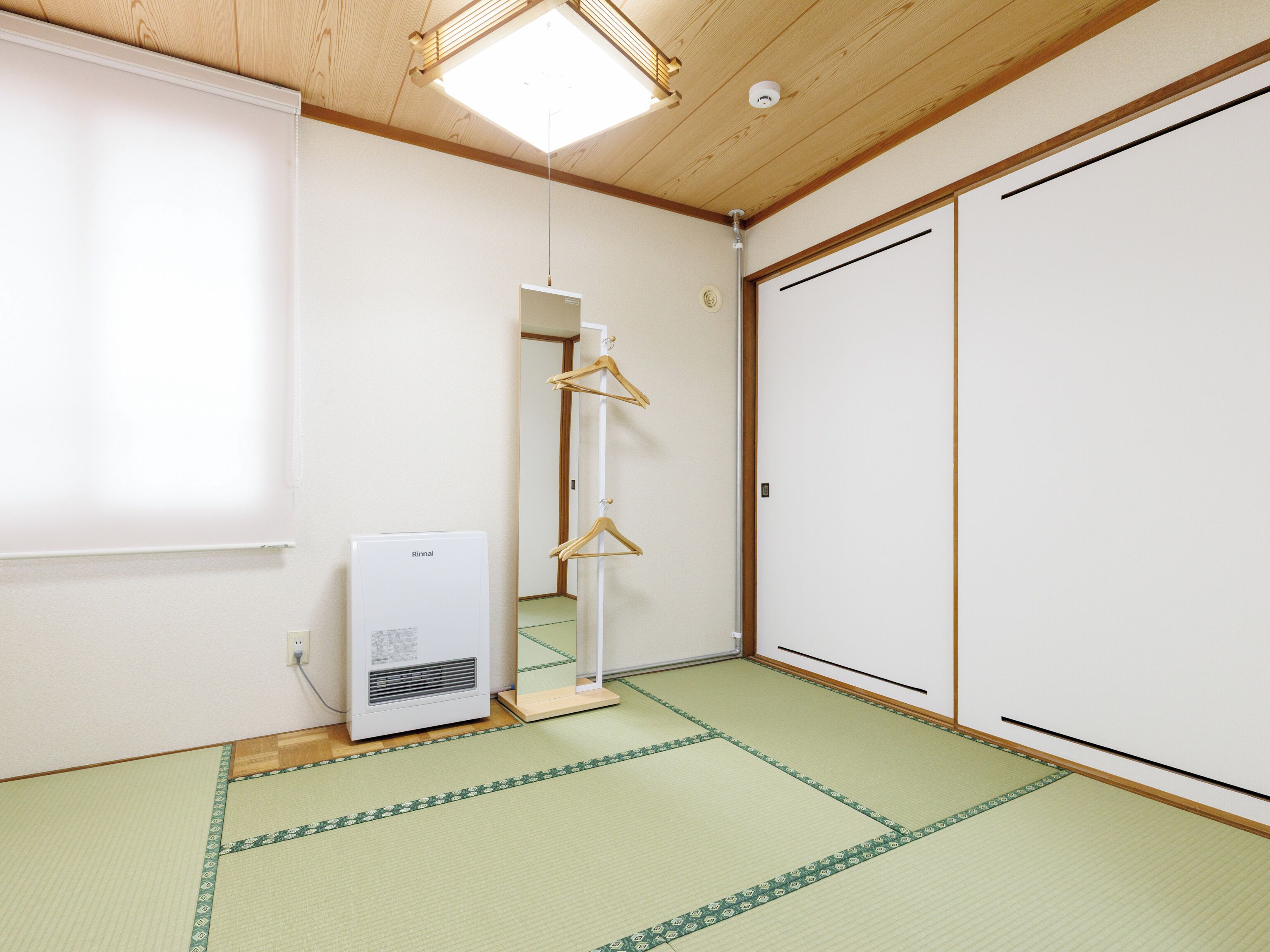 Quarto com piso de tatame, aquecedor, guarda-roupa e espelho com suporte de cabides de madeira.