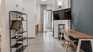 Quarto moderno e bem iluminado com uma escrivaninha de madeira, uma estante e uma televisão de tela plana.