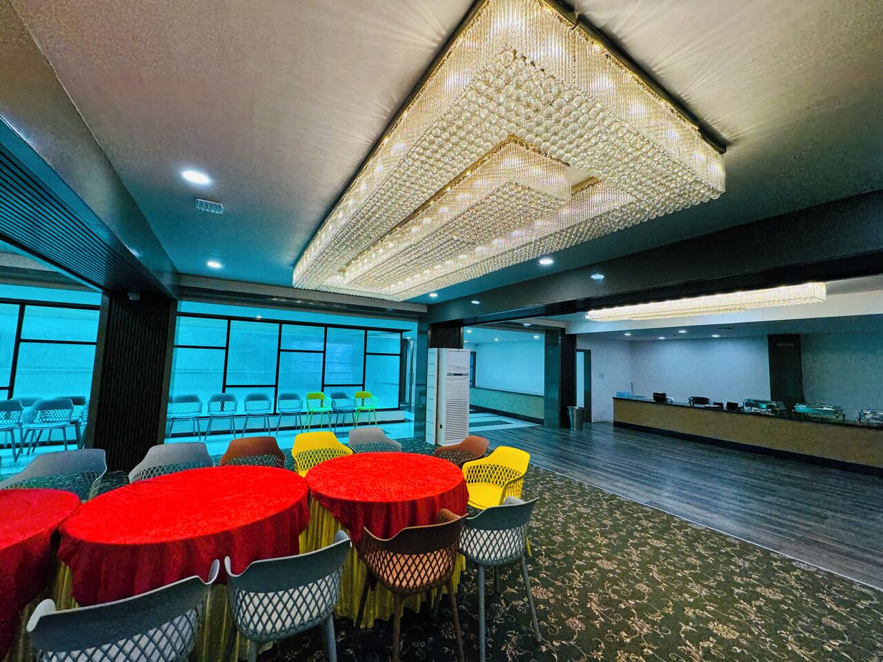 Uma sala de conferências com mesas redondas, cadeiras, um balcão de recepção e um lustre grande.