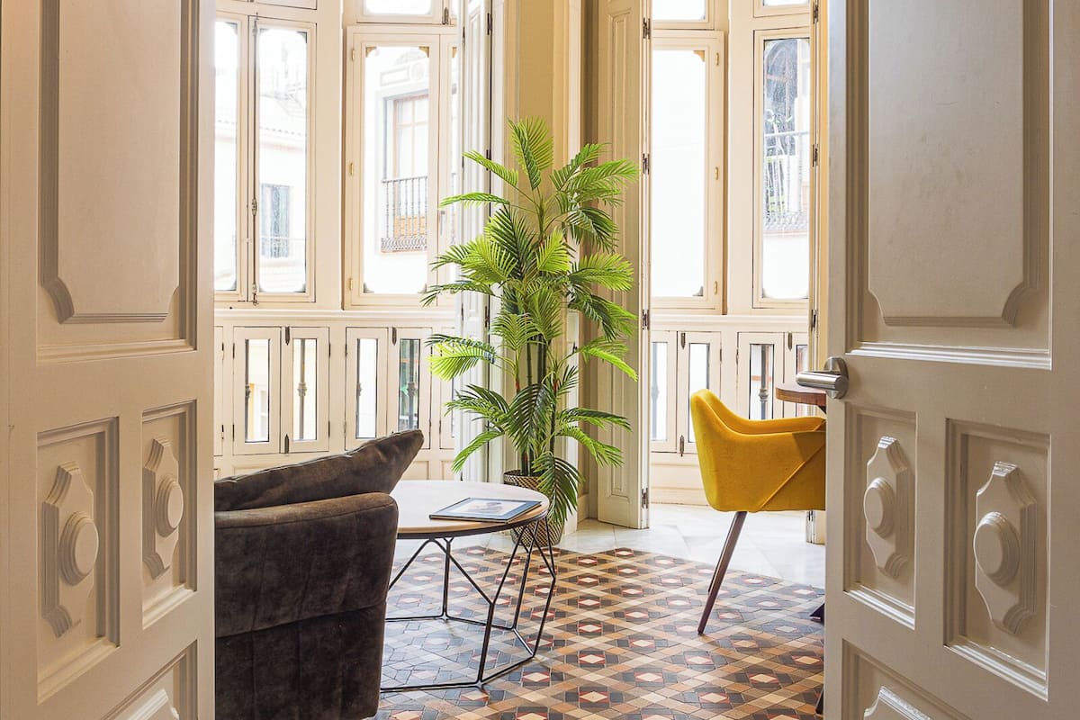Um corredor com piso estampado, uma planta em vaso e duas cadeiras.