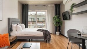Quarto de hotel moderno com cama, mesa de cabeceira, laptop e vista da cidade através de grandes janelas.