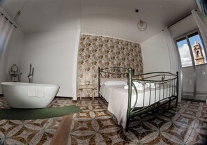 Quarto com cama, banheira, toucador e janela com vista para uma torre.