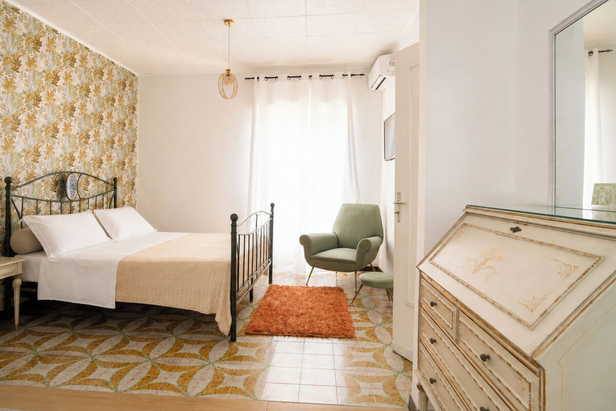 Quarto com cama, cadeira, cômoda e parede estampada.