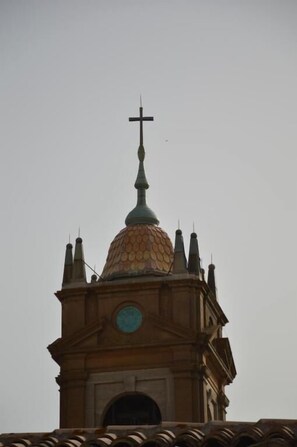 Uma torre de igreja com cruz no topo, um relógio e uma cúpula.