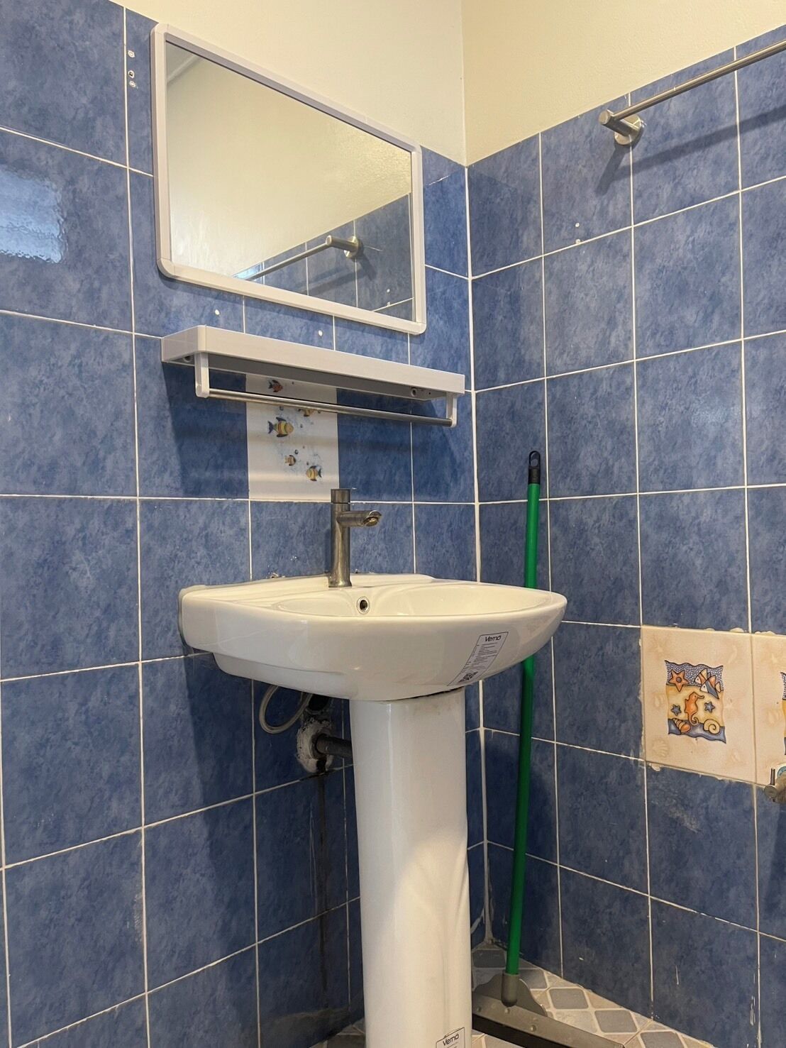 Casa de banho com lavatório pedestal branco, espelho em cima e azulejos azuis nas paredes.