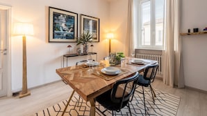 Uma área de jantar com uma mesa de madeira posta para quatro pessoas, duas luminárias fixadas na parede e obras de arte emolduradas acima.