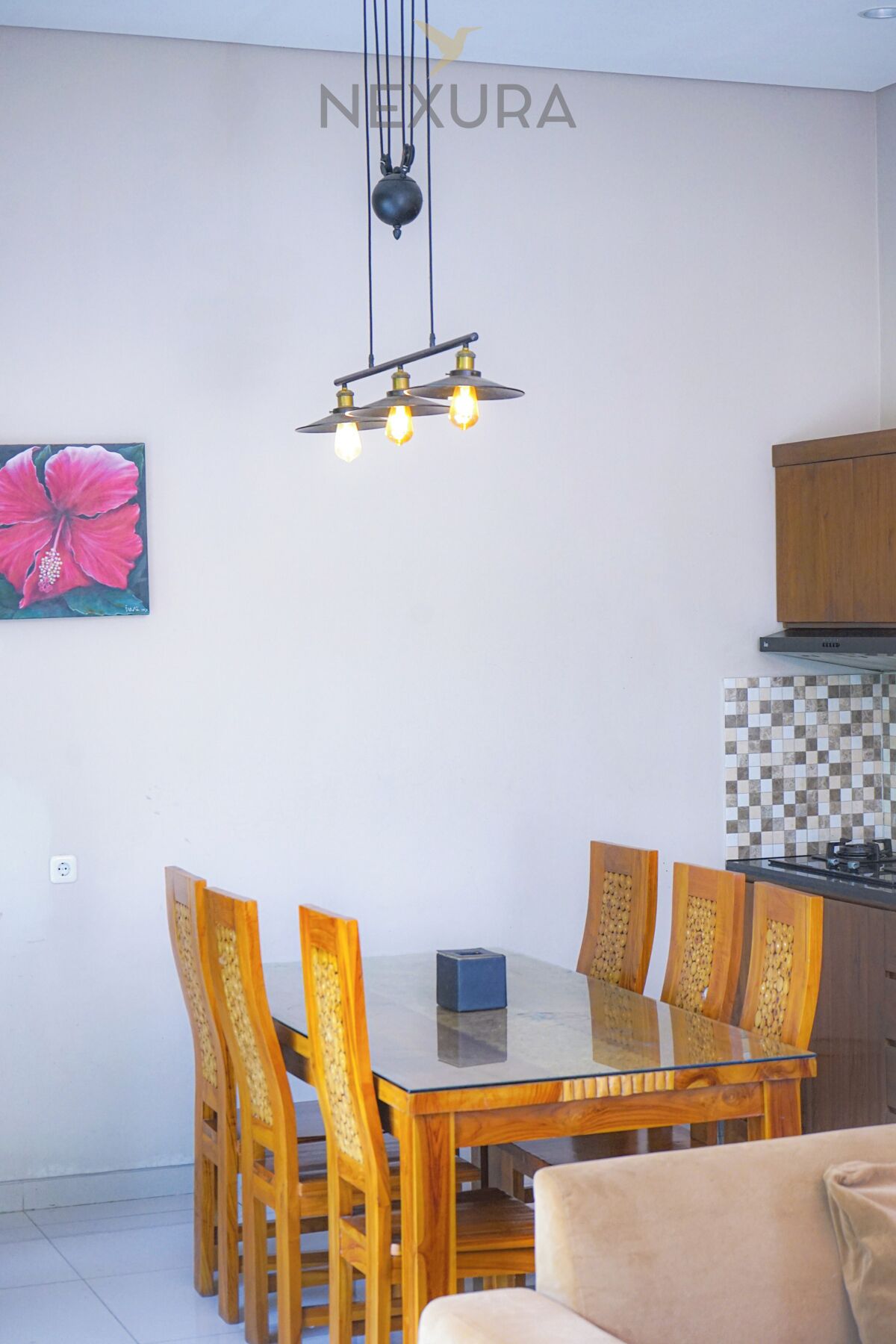 Uma área de refeições com mesa de vidro, cadeiras de madeira e luminária pendente.