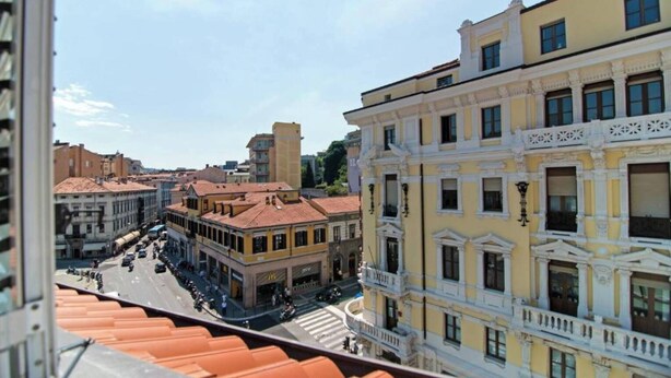 Vista da rua com edifícios, incluindo um edifício amarelo com varandas e um edifício com telhado vermelho.