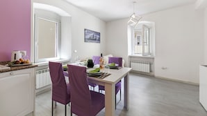 Uma área de refeições moderna com uma mesa branca, cadeiras roxas e uma janela com vista.