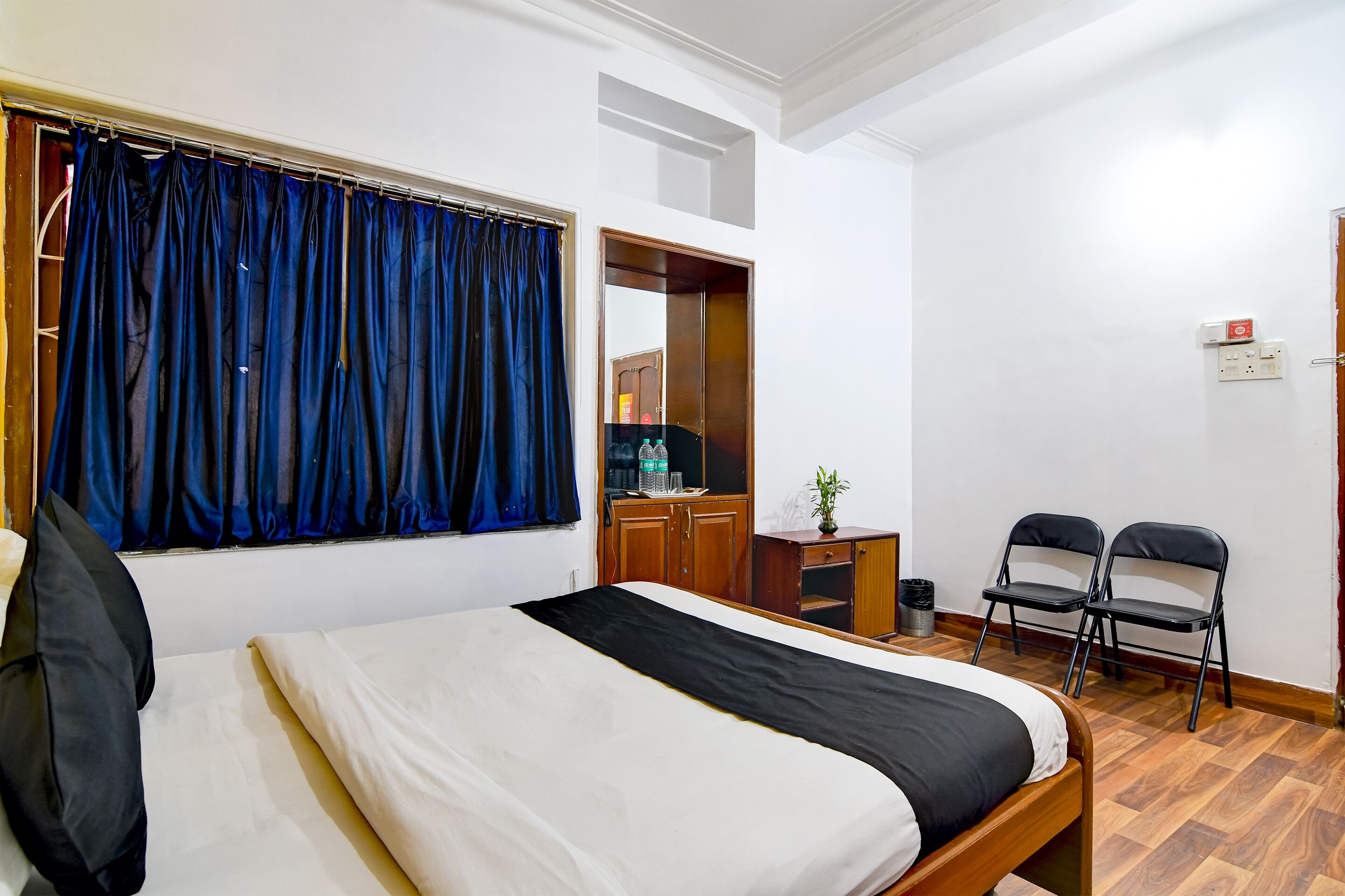 Quarto com cama, escrivaninha, duas cadeiras, guarda-roupa e janela com cortinas.