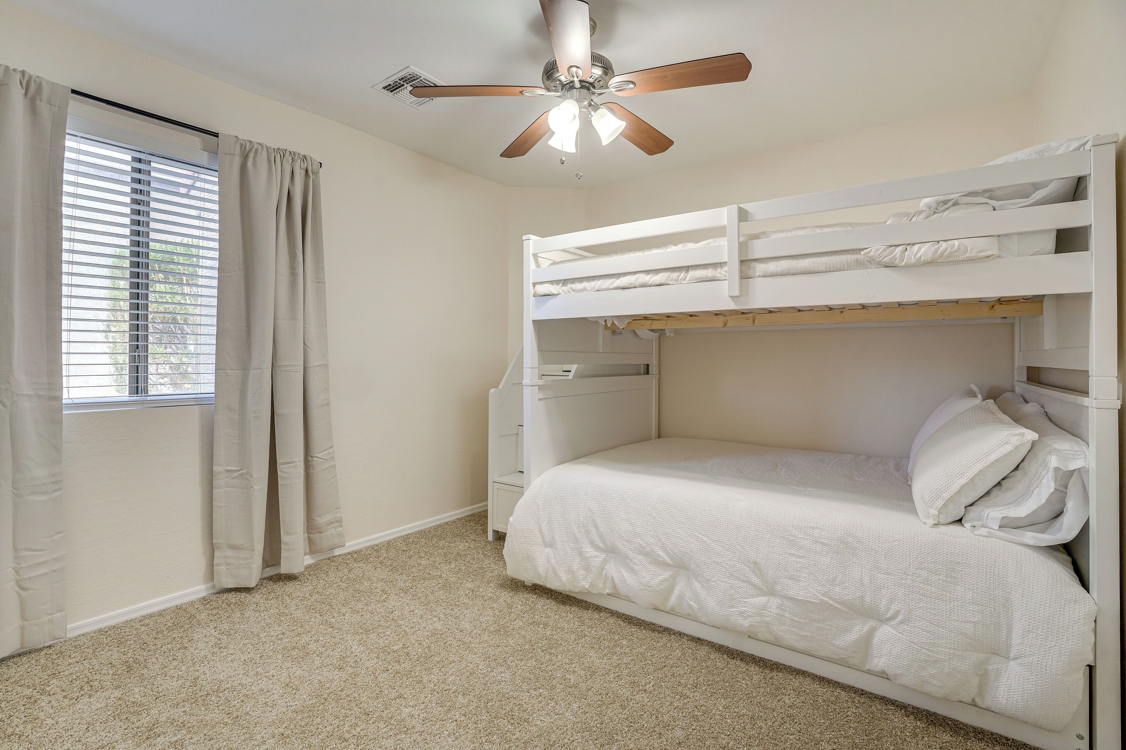 Quarto com beliche, ventoinha no teto, janela com cortinas e piso coberto por carpete.