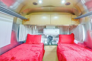 Quarto compacto e bem iluminado com duas camas, uma mesinha e um ventilador de teto.
