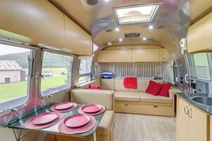 Interior compacto de uma RV com cozinha compacta, área de refeições e um pequeno espaço de estar com sofá e almofadas.