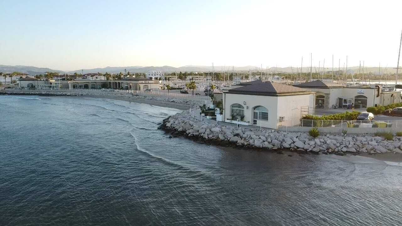 Um edifício costeiro com fachada branca, parede de pedra e vista para o mar.