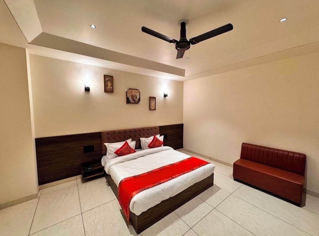 Quarto moderno com uma cama grande, um banco vermelho, ventilador de teto e luminárias fixadas na parede.