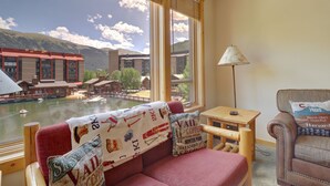 Um quarto aconchegante com vista para um rio e edifícios, uma mesa de madeira e um sofá com almofadas decorativas.