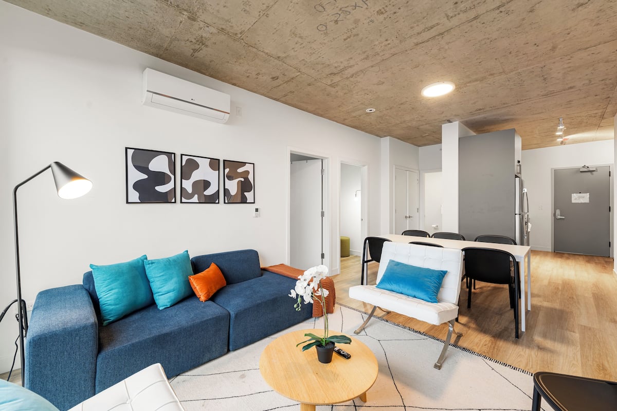 Uma sala de estar moderna com um sofá azul, poltronas brancas e uma área de jantar com mesa e cadeiras.