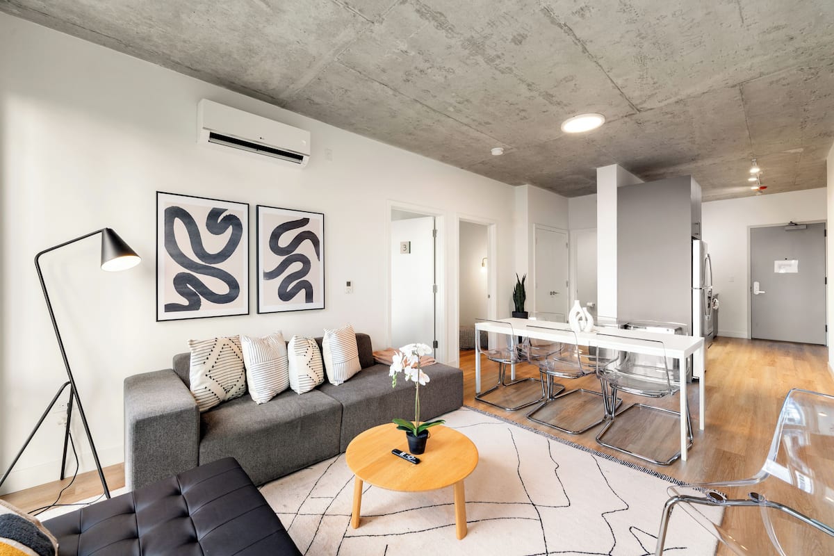 Uma sala de estar moderna com um sofá cinzento, uma mesa de centro redonda com uma planta e arte abstrata na parede.