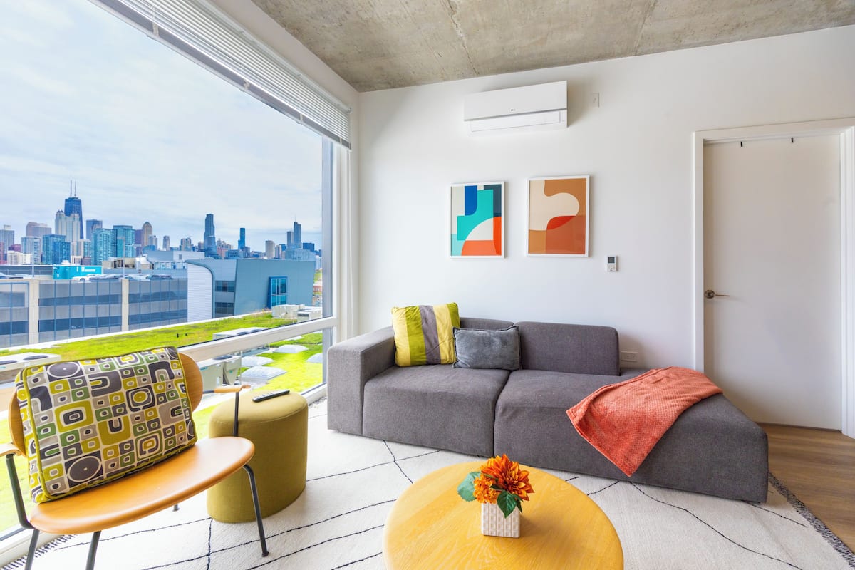 Uma sala de estar moderna com um sofá cinzento, uma poltrona amarela e uma mesa de centro redonda com um vaso de flores.