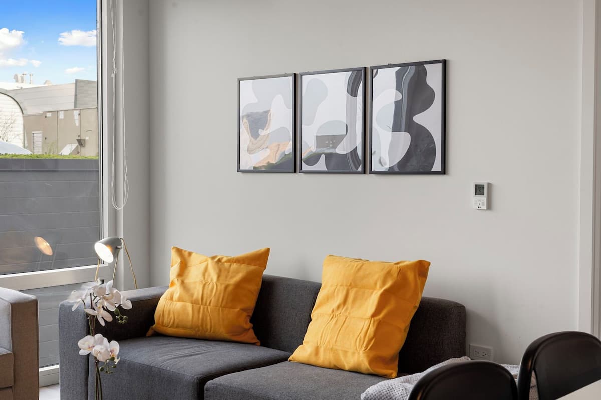 Uma sala de estar moderna com um sofá cinzento, duas almofadas amarelo mostarda e uma obra de arte abstrata na parede.