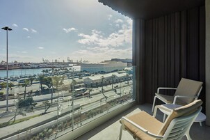 Varanda com vista para um porto, um estacionamento e uma autoestrada. Há duas cadeiras brancas com almofadas.