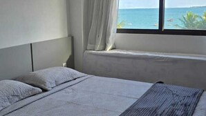 Quarto de hotel com uma cama grande, janela com vista para o mar e uma luminária no teto.
