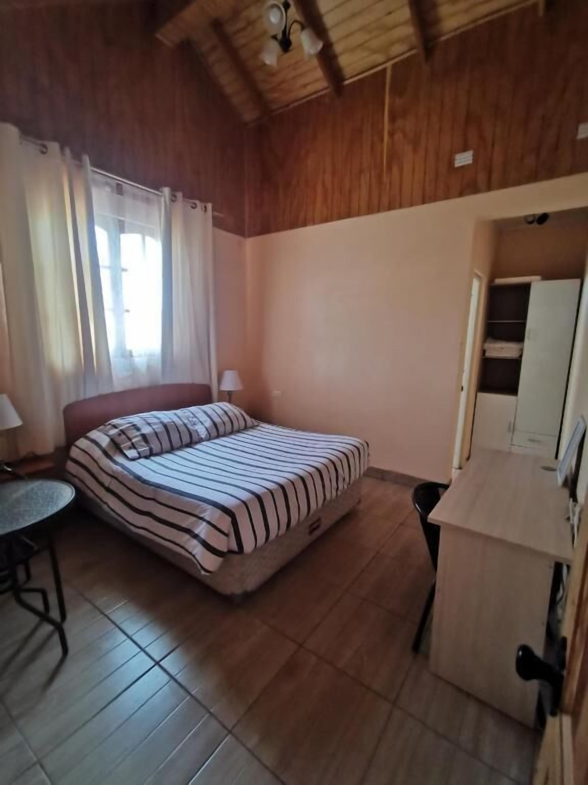 Um quarto com uma cama, uma escrivaninha, uma cadeira e um guarda-roupa.